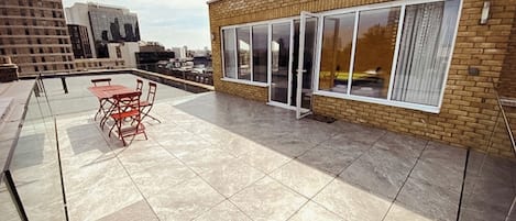 Terraço no terraço com mesa e cadeiras, porta de vidro e vista para a cidade.
