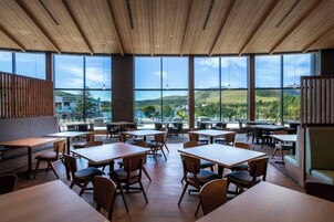 Restaurante com grandes janelas, teto de madeira e várias mesas e cadeiras.