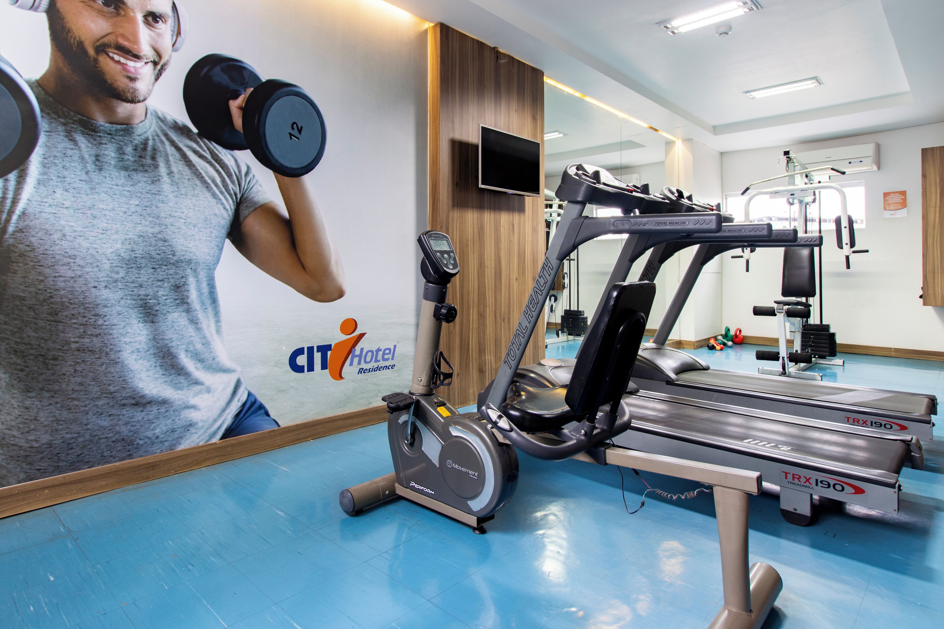 Uma academia com equipamentos de ginástica, incluindo halteres, uma bicicleta ergométrica e uma esteira.