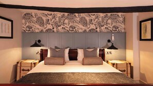 Uma cama bem arrumada com um cobertor cinza, duas mesas de cabeceira com abajures e um painel de cama com padrão floral.