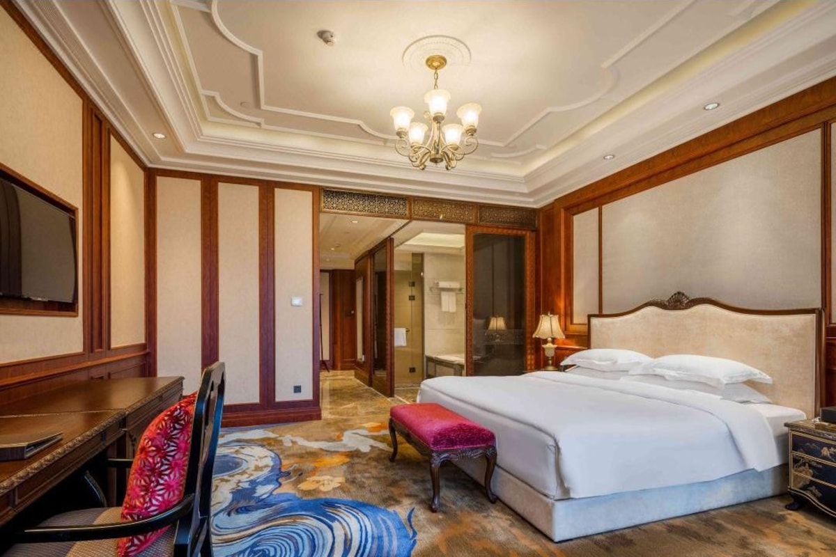 Quarto de hotel com cama, escrivaninha, cadeira, televisão e tapete.