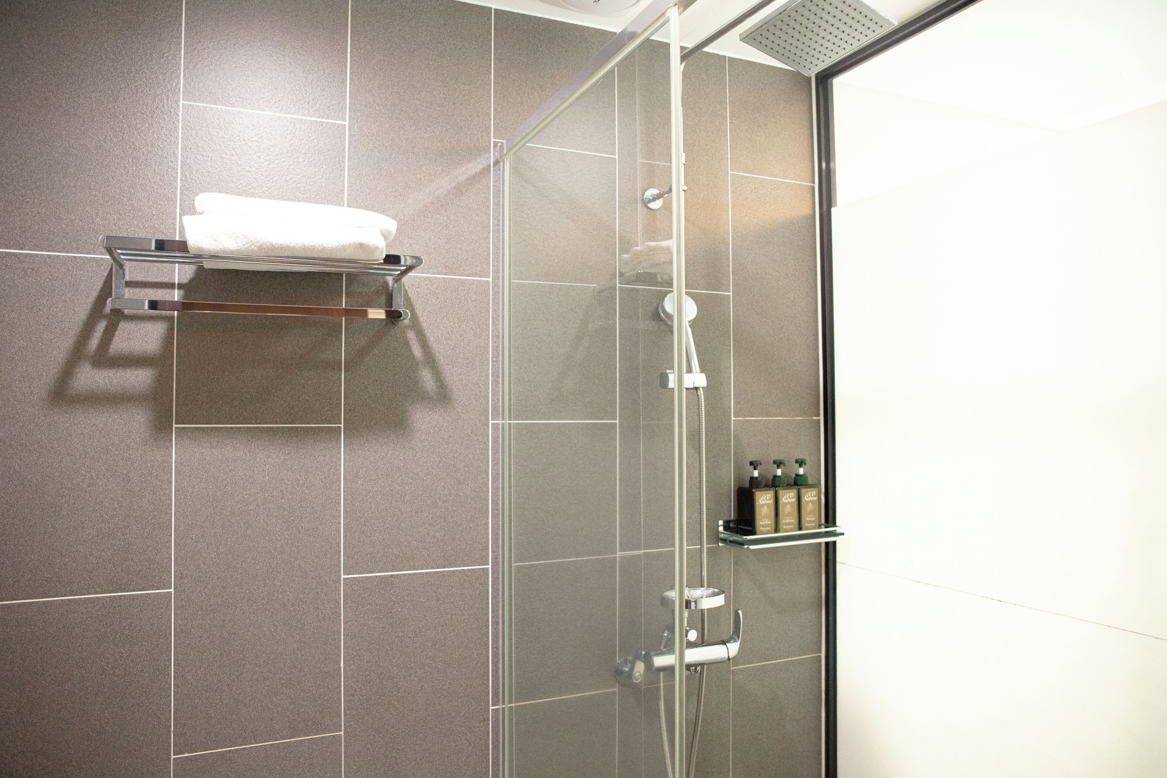 Uma área de chuveiro moderna com porta de vidro, um porta-toalhas e um prateleira com produtos de higiene pessoal.