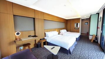 Quarto de hotel com duas camas, uma escrivaninha com um laptop, uma mesinha pequena e um sofá roxo.