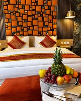 Quarto de hotel com uma cama, uma cesta de frutas ao lado e um detalhe decorativo na parede.