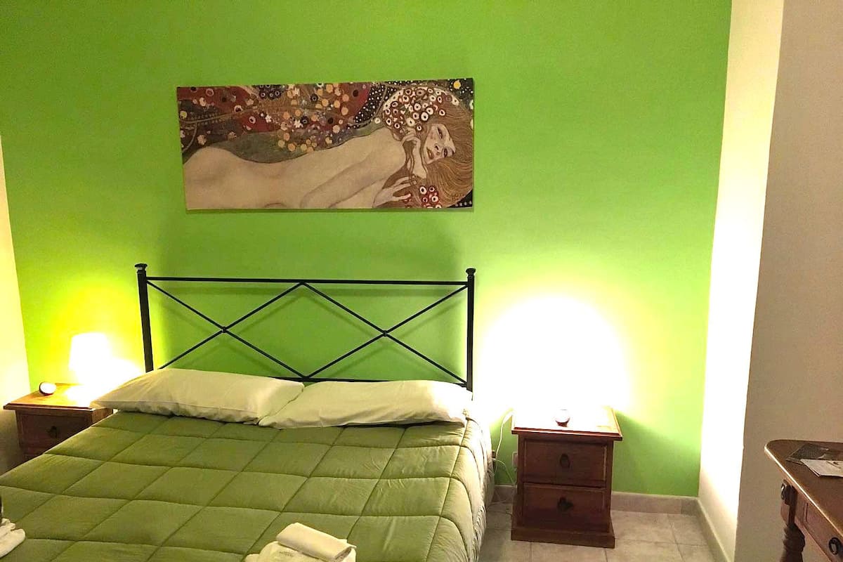 Uma cama com um edredom verde, duas mesas de cabeceira com luminárias e um quadro na parede.