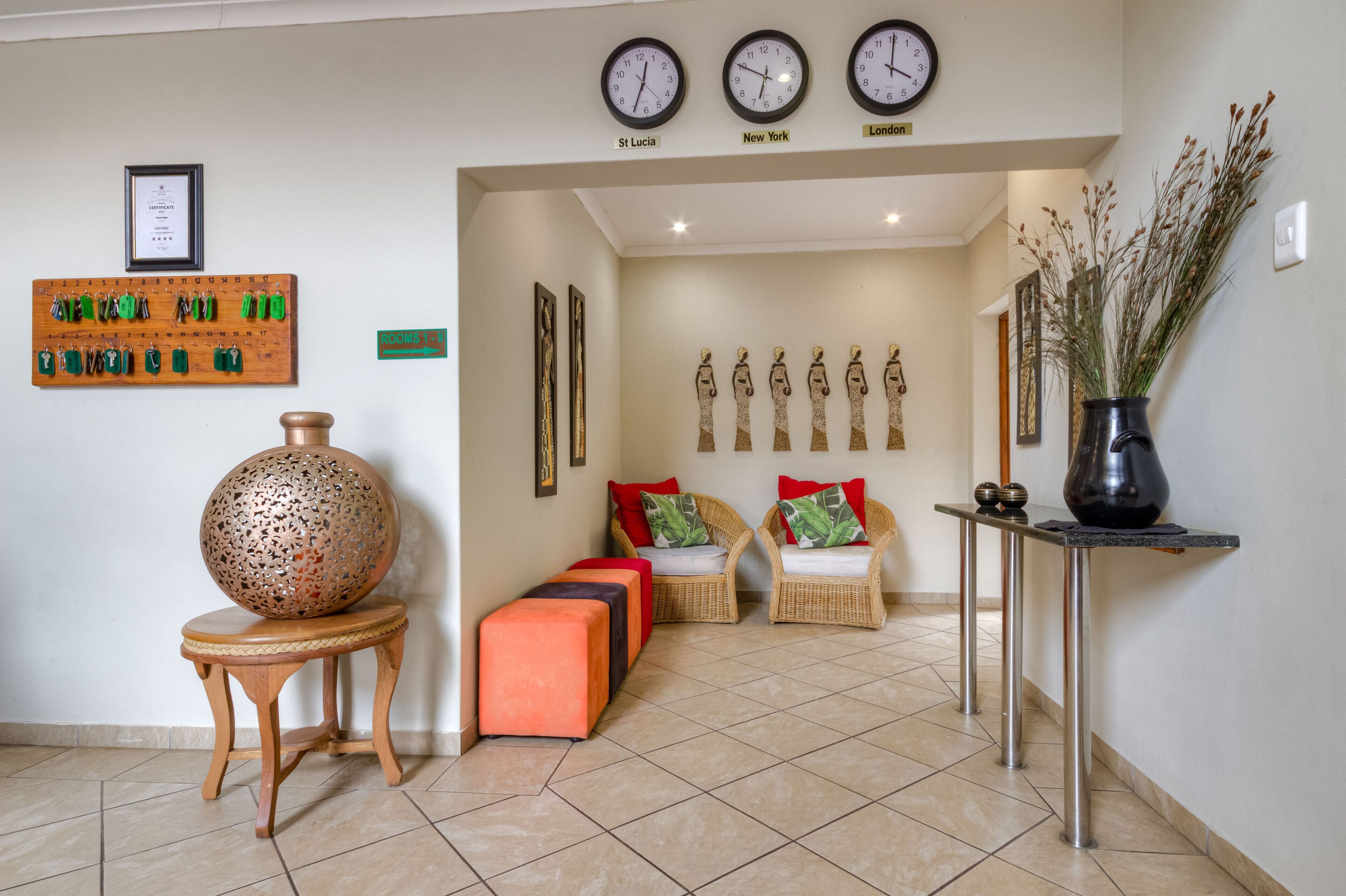 Um hall com balcão de recepção, um vaso grande, cadeiras de vime, um relógio e um certificado emoldurado.