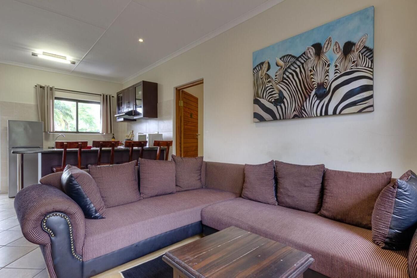 Uma sala de estar com sofá seccional, mesa de centro e um quadro de zebras na parede.
