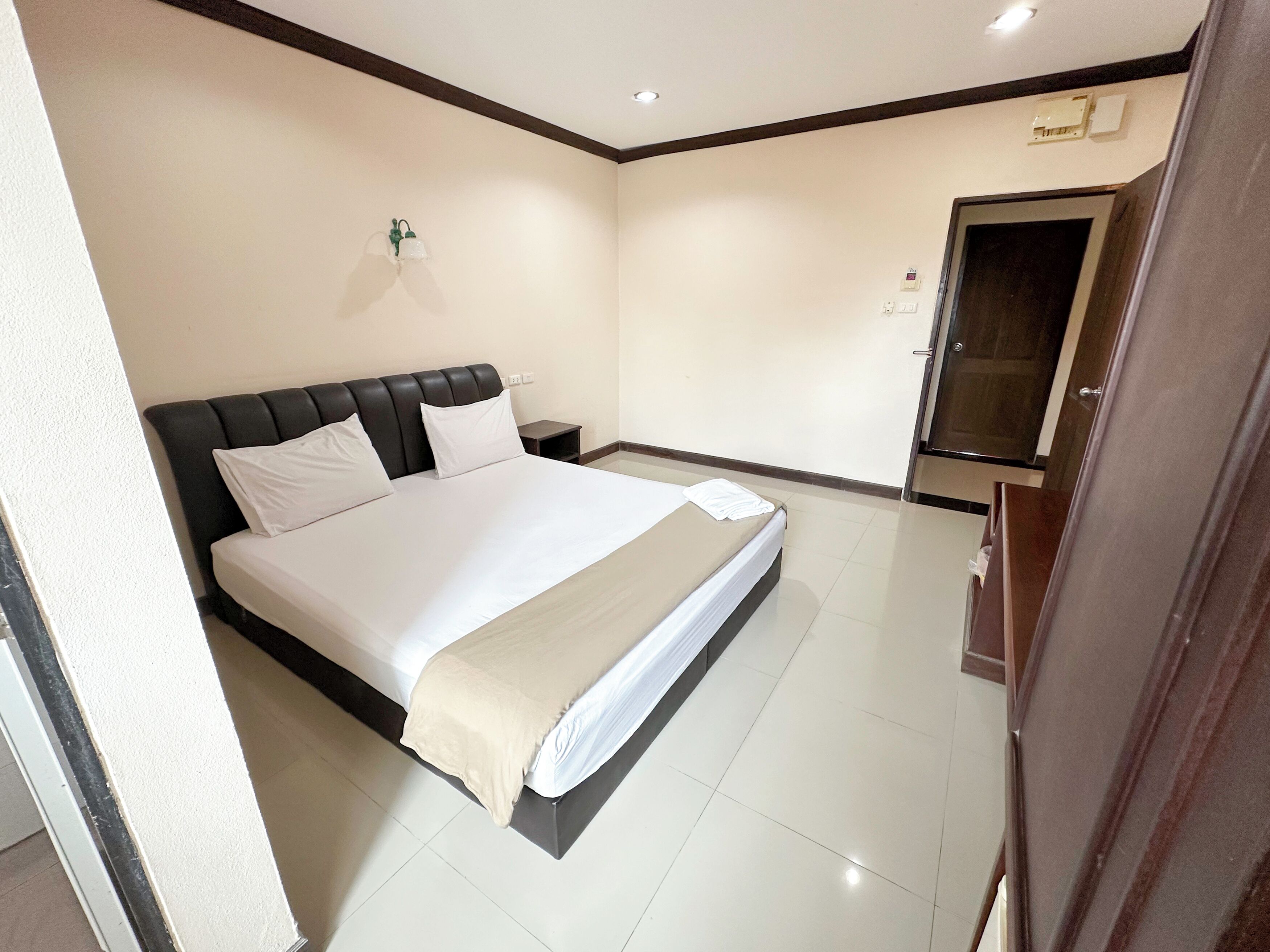Quarto de hotel com cama, mesa de cabeceira, guarda-roupa e luminária na parede.
