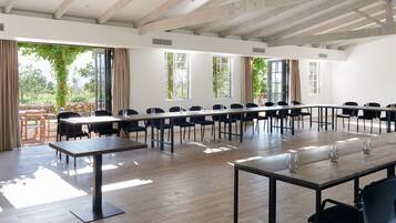Uma sala de conferências com mesas compridas e cadeiras, janelas amplas e teto de madeira.