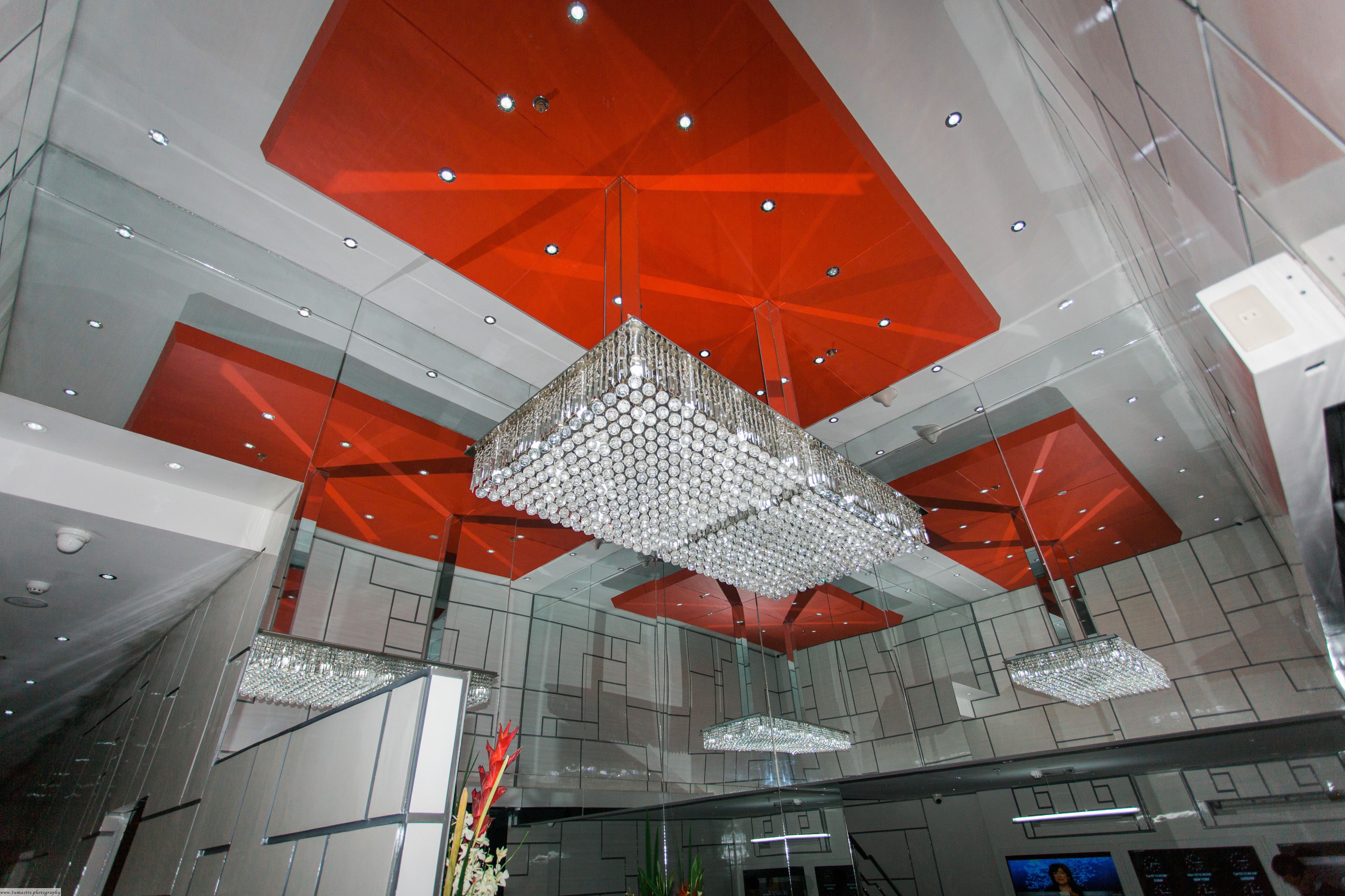Um interior moderno com design geométrico no teto, superfícies refletoras e lustres de cristal pendentes.