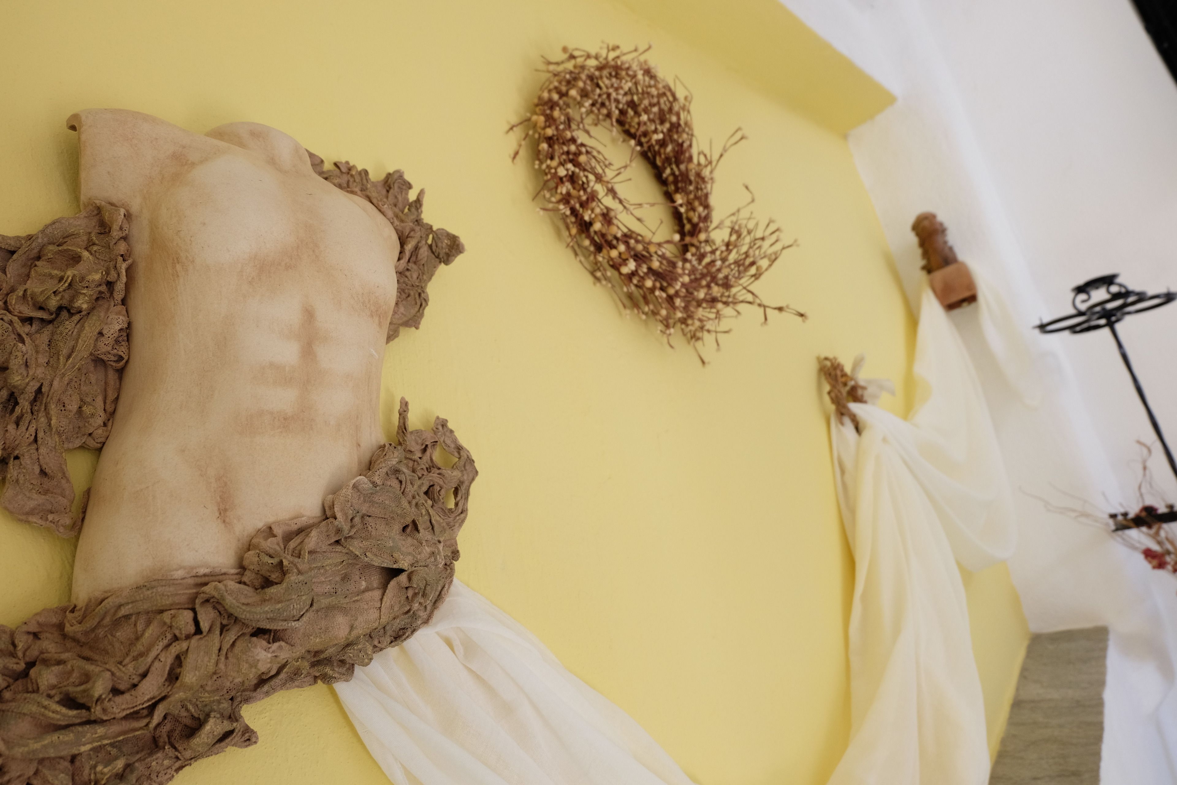 Um quarto com parede amarela, cortina branca e tecido branco sobre uma cadeira de madeira.