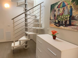 Escada moderna com corrimão de metal, parede branca com uma pintura e uma pequena planta em vaso sobre um balcão branco.