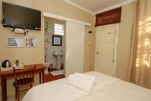 Quarto de hotel com uma cama, uma escrivaninha com cadeira, televisão e banheiro visível por uma porta aberta.