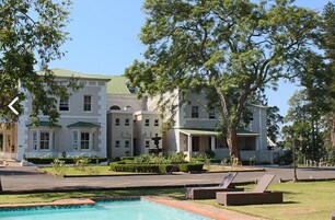 Um edifício grande com piscina, rodeado por árvores e um relvado bem cuidado.