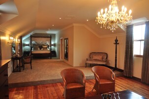 Um quarto espaçoso com uma cama grande, um espaço de estar com cadeiras de vime, um candelabro e vista para o exterior.
