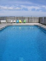 Piscina retangular com deck de madeira e cerca de madeira ao fundo.