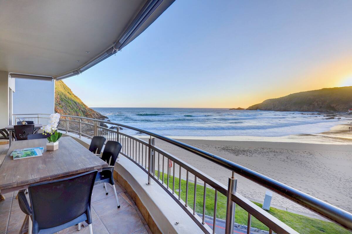 Uma varanda com vista para o oceano e uma mesa de madeira com cadeiras.