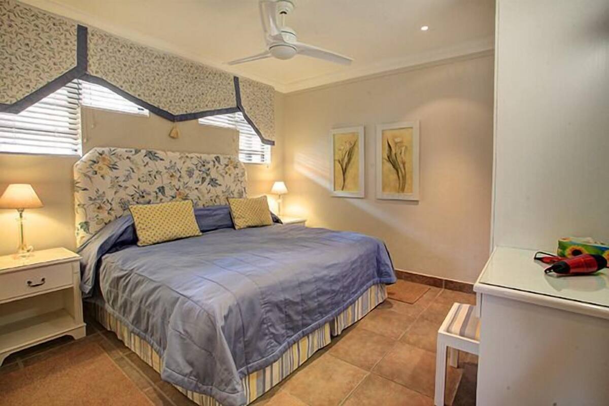 Quarto com cama, mesas de cabeceira, ventoinha no teto e obras de arte na parede.