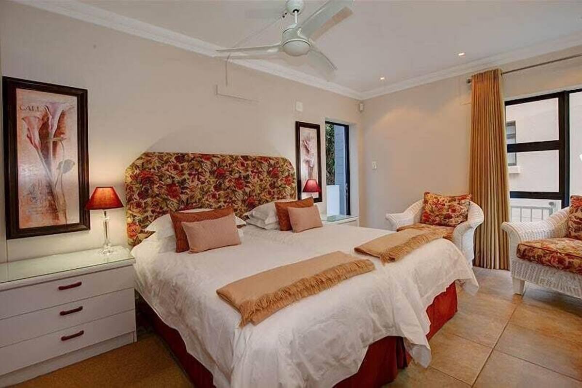 Quarto com uma cama grande, duas mesas de cabeceira, um ventilador de teto e uma janela com cortinas.