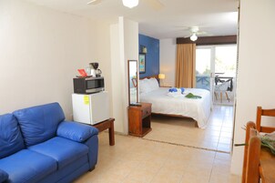 Quarto de hotel com sofá azul, cama, mesa pequena, micro-ondas e varanda com vista.