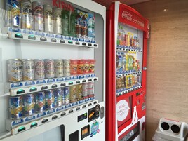 Máquina automática com diversas bebidas e petiscos, incluindo cerveja Kirin, água e Coca-Cola.