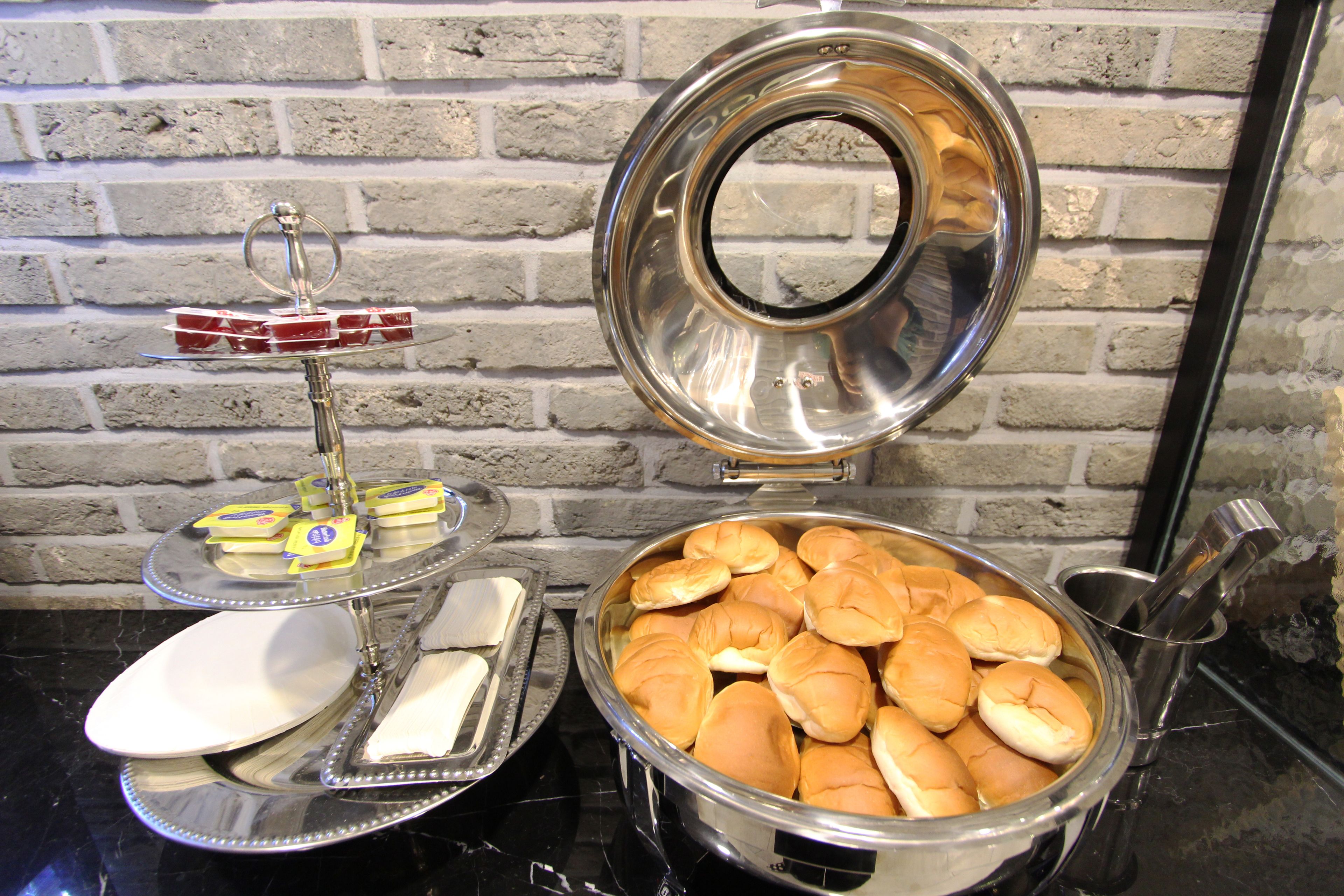 Disposição de buffet com bandejas de comida, incluindo pães e bandejas de manteiga e queijo.