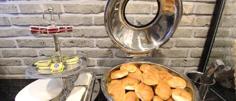 Disposição de buffet com bandejas de comida, incluindo pães e bandejas de manteiga e queijo.