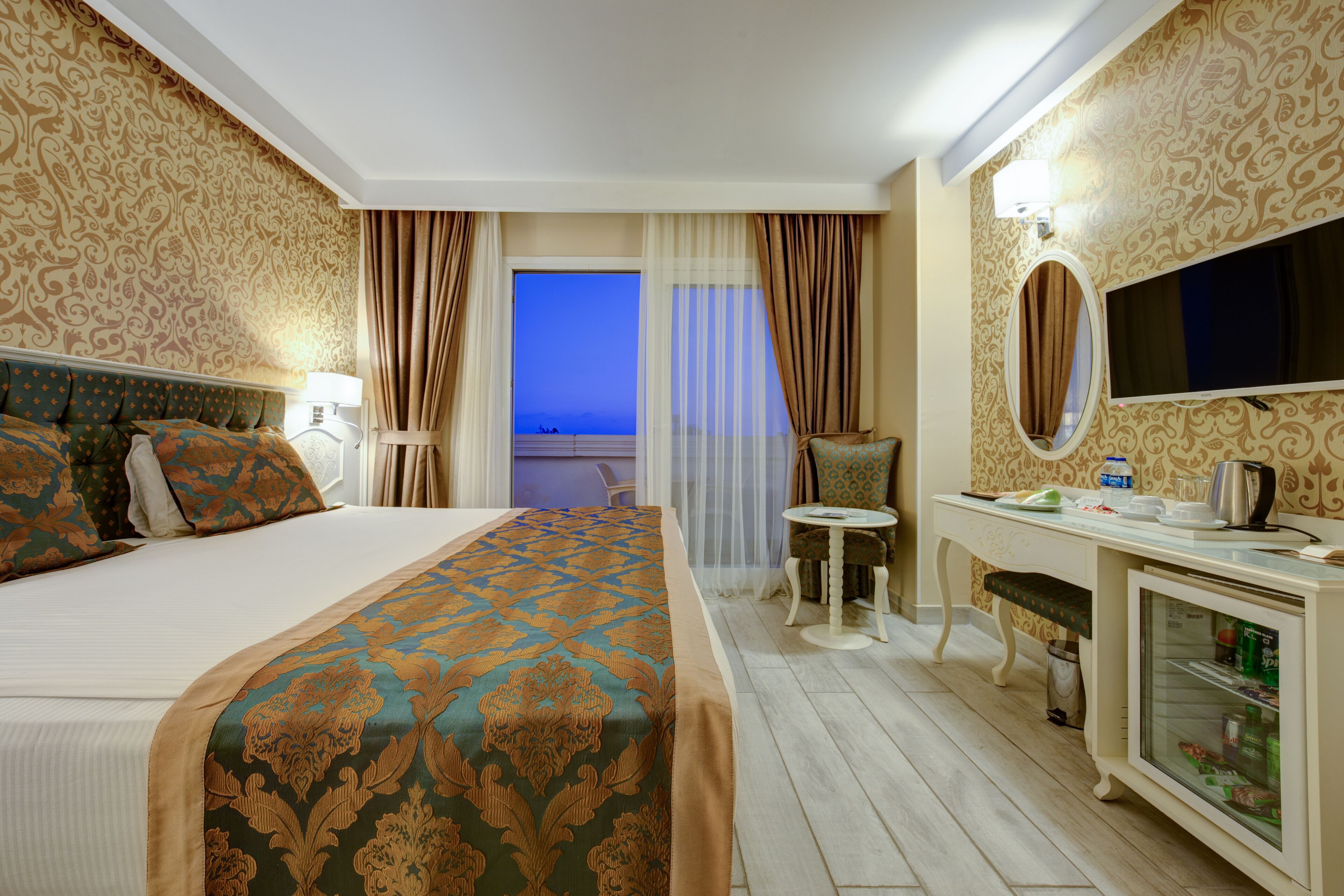 Quarto de hotel com uma cama grande, uma escrivaninha com espelho, uma mesinha e vista para o mar.