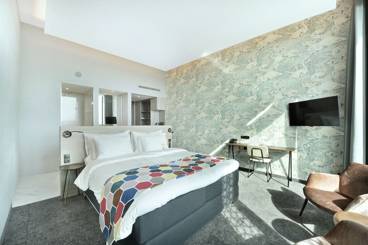 Quarto de hotel moderno com cama grande, escrivaninha e televisão.