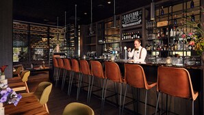 Uma área de bar com um bartender, balcão de madeira e assentos.