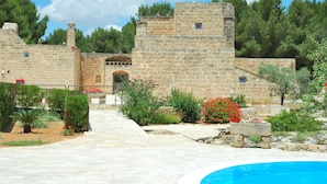 Um edifício de pedra com piscina, cercado por vegetação e céu claro.