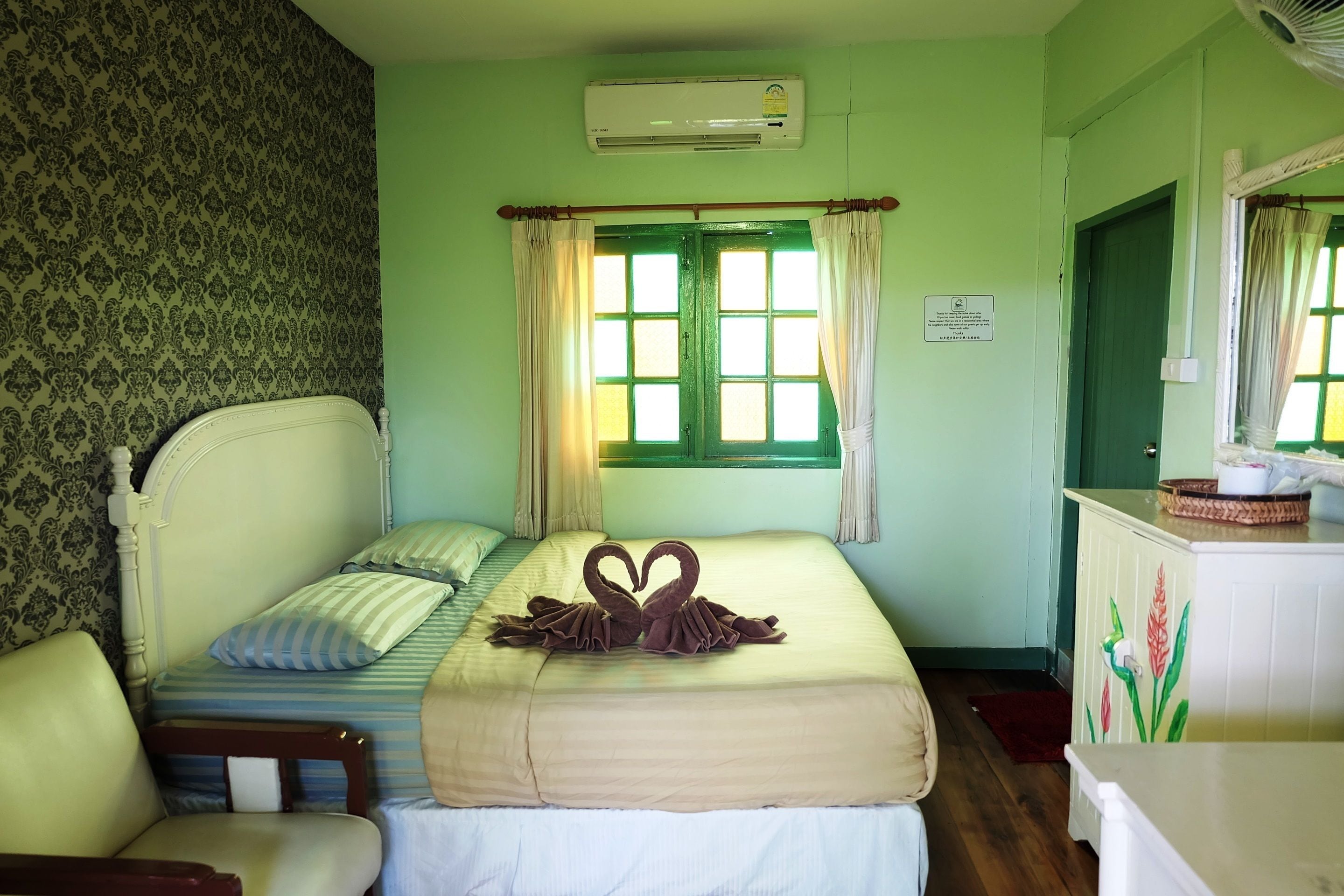 Quarto com cama, uma cadeira, janela com cortinas, ar-condicionado fixado na parede e um armário com espelho.
