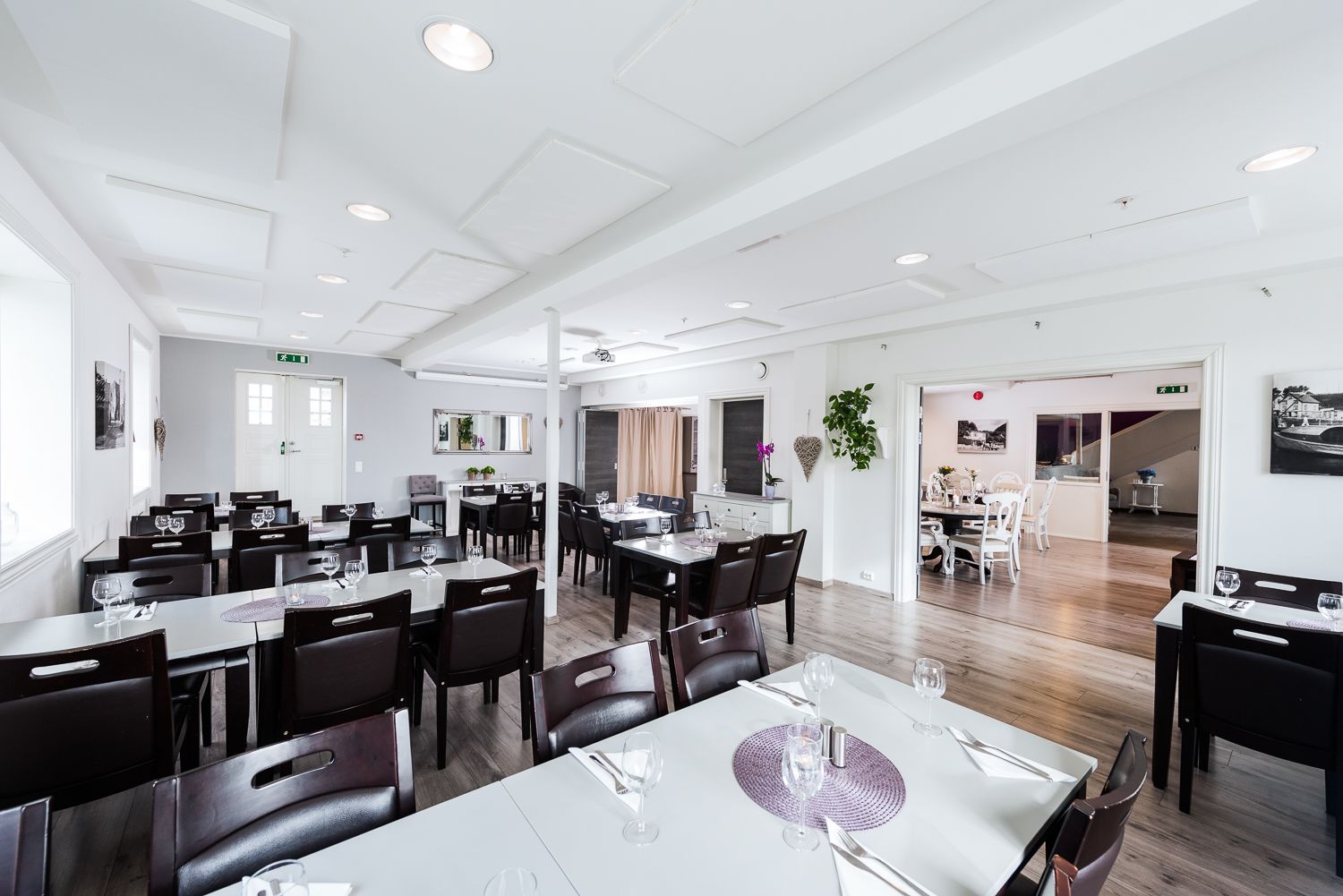 Uma sala de jantar ampla com várias mesas e cadeiras, um design de teto moderno e vista para o quarto adjacente.
