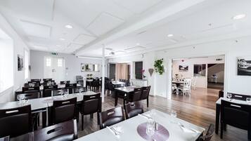 Uma sala de jantar ampla com várias mesas e cadeiras, um design de teto moderno e vista para o quarto adjacente.