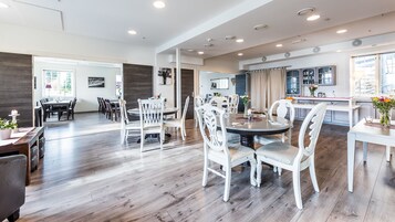 Uma sala de jantar ampla, com cadeiras brancas estofadas e uma mesa redonda, uma cozinha com eletrodomésticos modernos e uma janela grande que oferece iluminação natural.