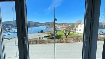 Vista pela janela de uma marina com barcos, um lago e uma área gramada com um prédio.