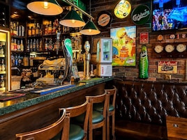 Uma área de bar com balcão, banquetas, máquina de café e diversos frascos e copos.