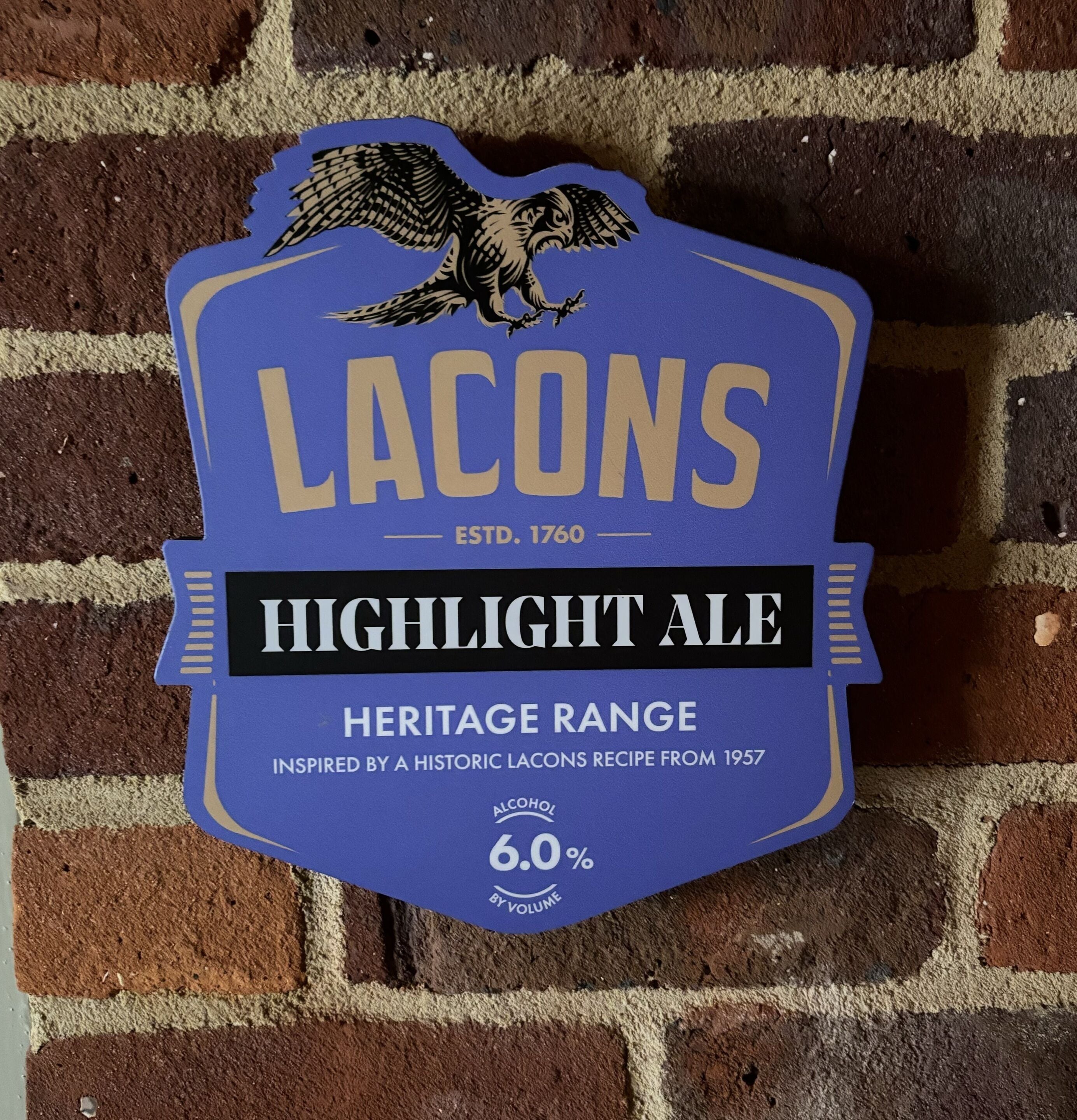 Uma placa azul com os dizeres 'Lacons' e 'Highlight Ale' em uma parede de tijolos.