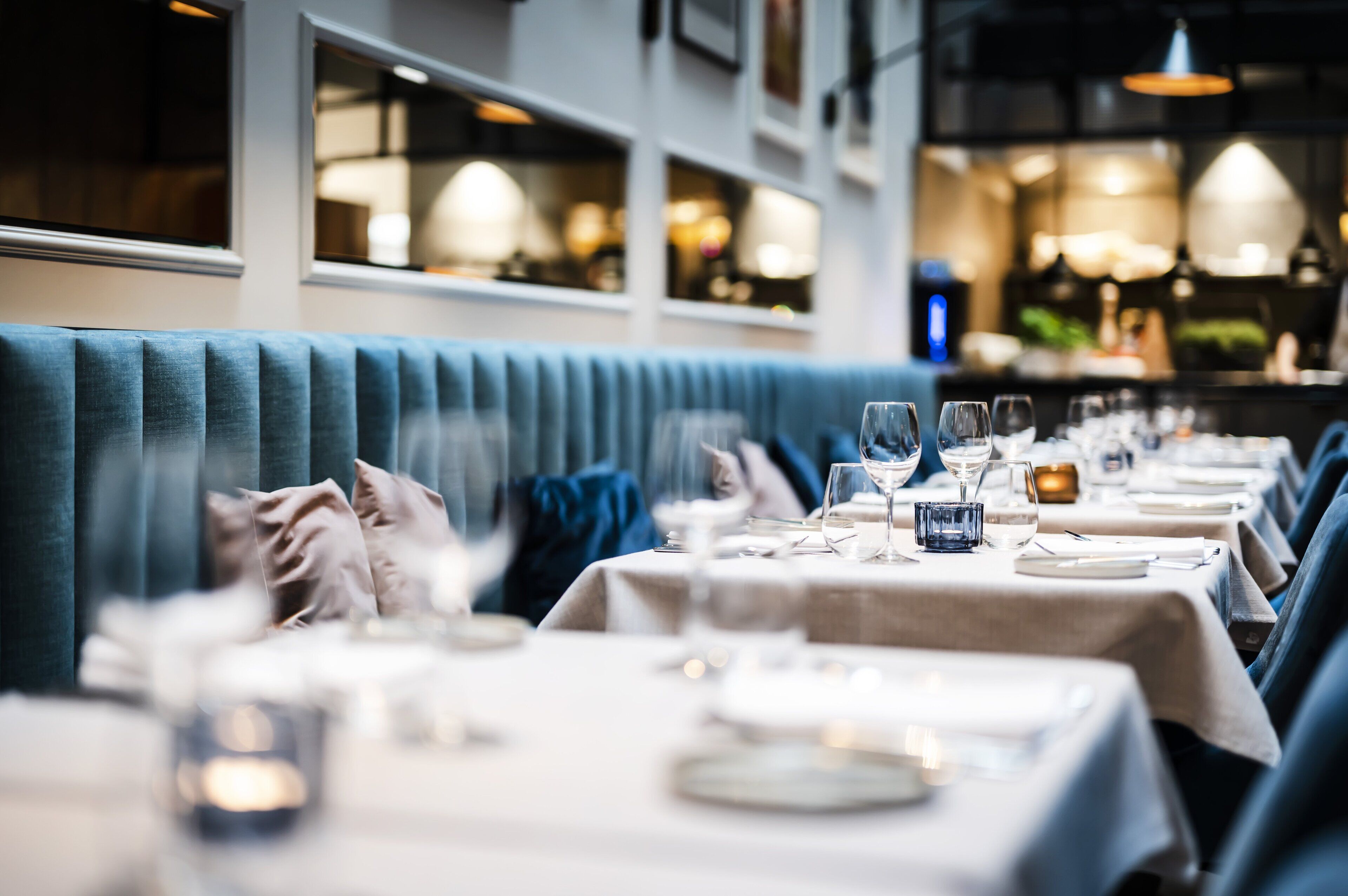 Restaurante com assentos estofados em azul, mesas bem arrumadas com toalhas brancas e copos.