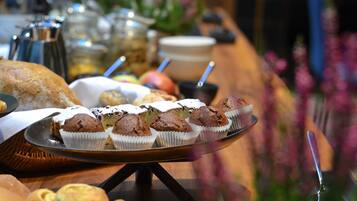 Uma bandeja com muffins e doces sobre uma mesa, com diversos alimentos e recipientes ao fundo.