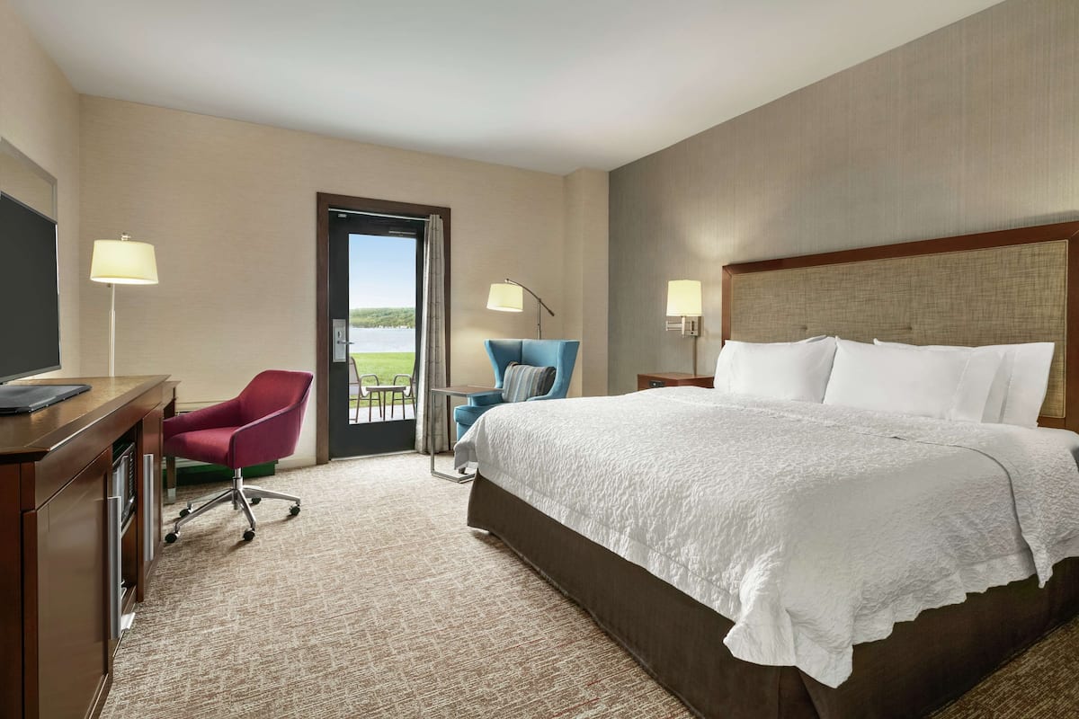 Quarto de hotel com uma cama grande, uma escrivaninha com cadeira, uma mesinha e vista para o exterior.