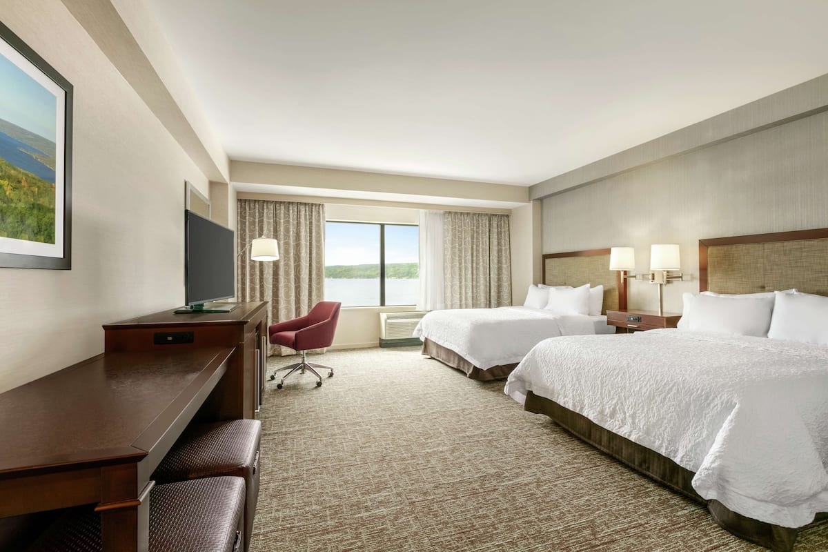 Quarto de hotel com duas camas, uma escrivaninha, uma cadeira e uma televisão.
