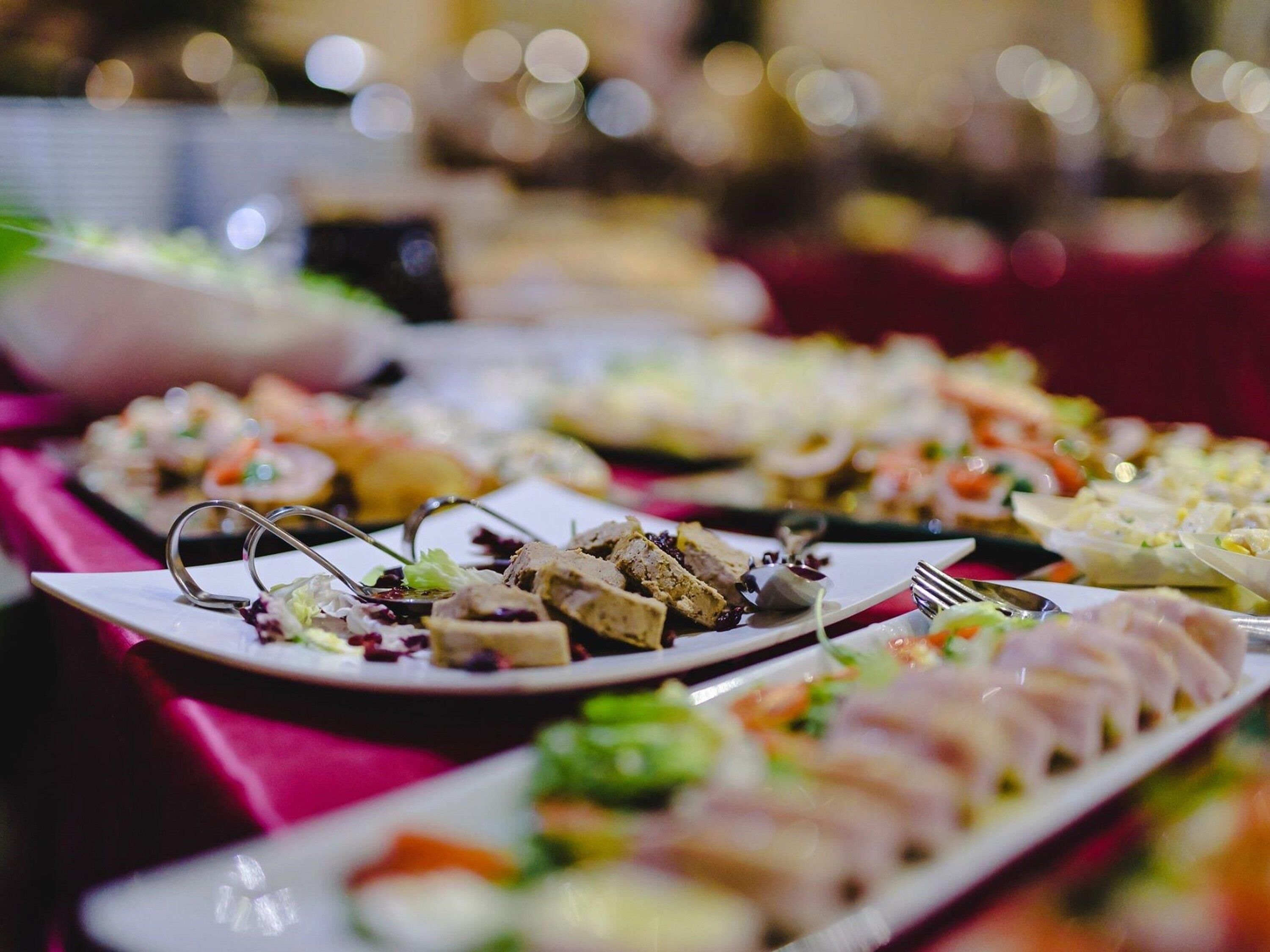 Uma mesa de buffet com diversos pratos, incluindo carnes fatiadas, saladas e aperitivos.
