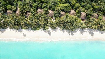 Vista aérea de uma praia com areia branca e águas azul-turquesa, cercada por vegetação verde exuberante e grandes rochas.