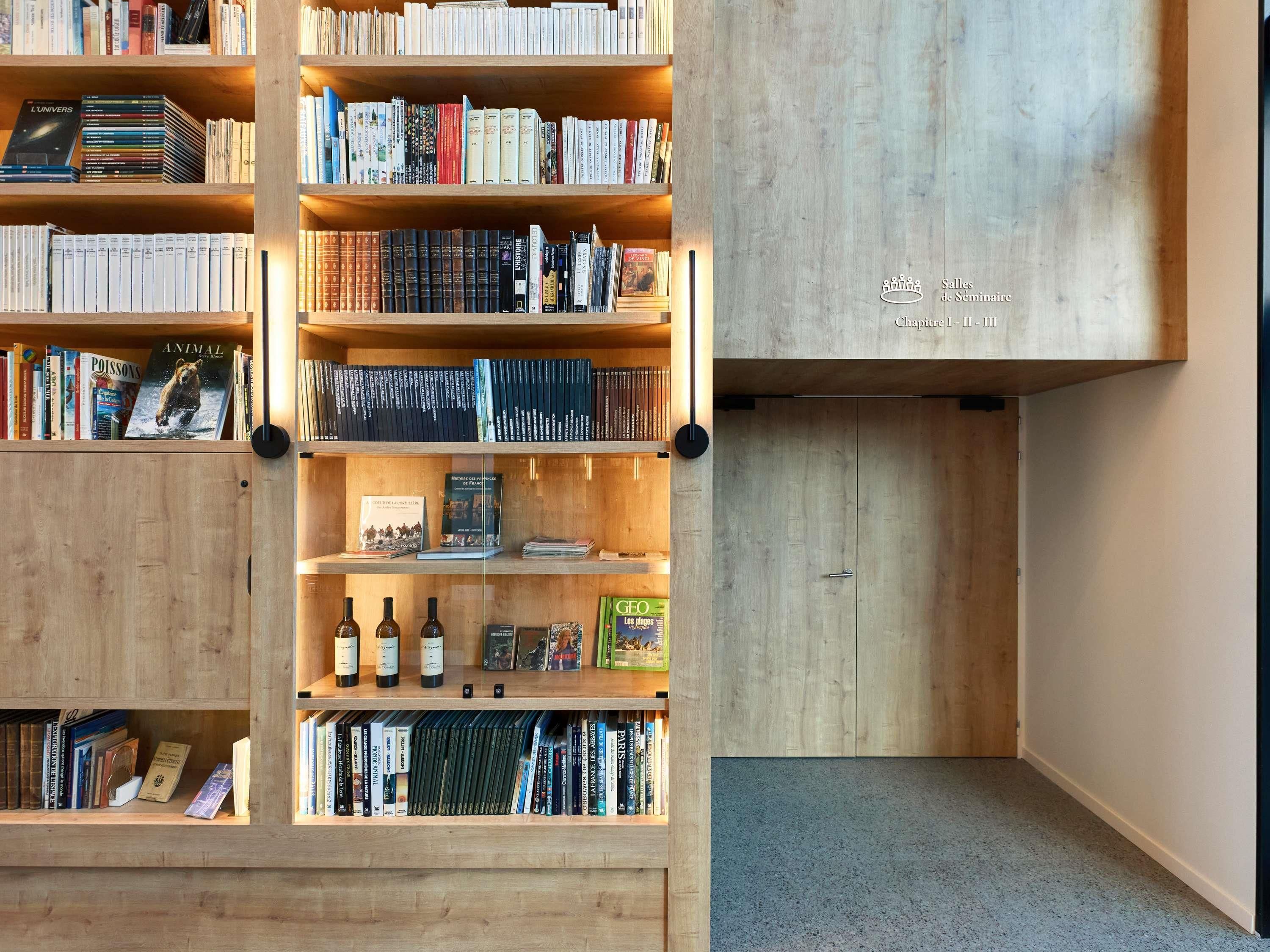 Uma biblioteca com estantes de madeira cheias de livros e algumas garrafas.