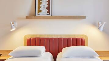 Quarto de hotel com cabeceira de madeira, duas camas com roupa de cama branca, uma obra de arte emoldurada acima da cabeceira e duas luminárias fixadas na parede.