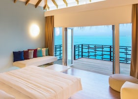 Quarto com cama grande, sofá e vista para o mar através de uma varanda.