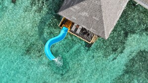 Uma cabana sobre a água com telhado de palha, um pequeno deque e um escorregador azul.
