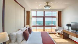 Quarto de hotel com uma janela grande, uma cama, uma escrivaninha com TV e uma cadeira.