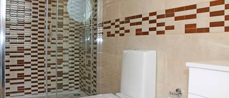 Casa de banho com cabine de duche em vidro, sanita e parede revestida a mosaicos com padrão xadrez.